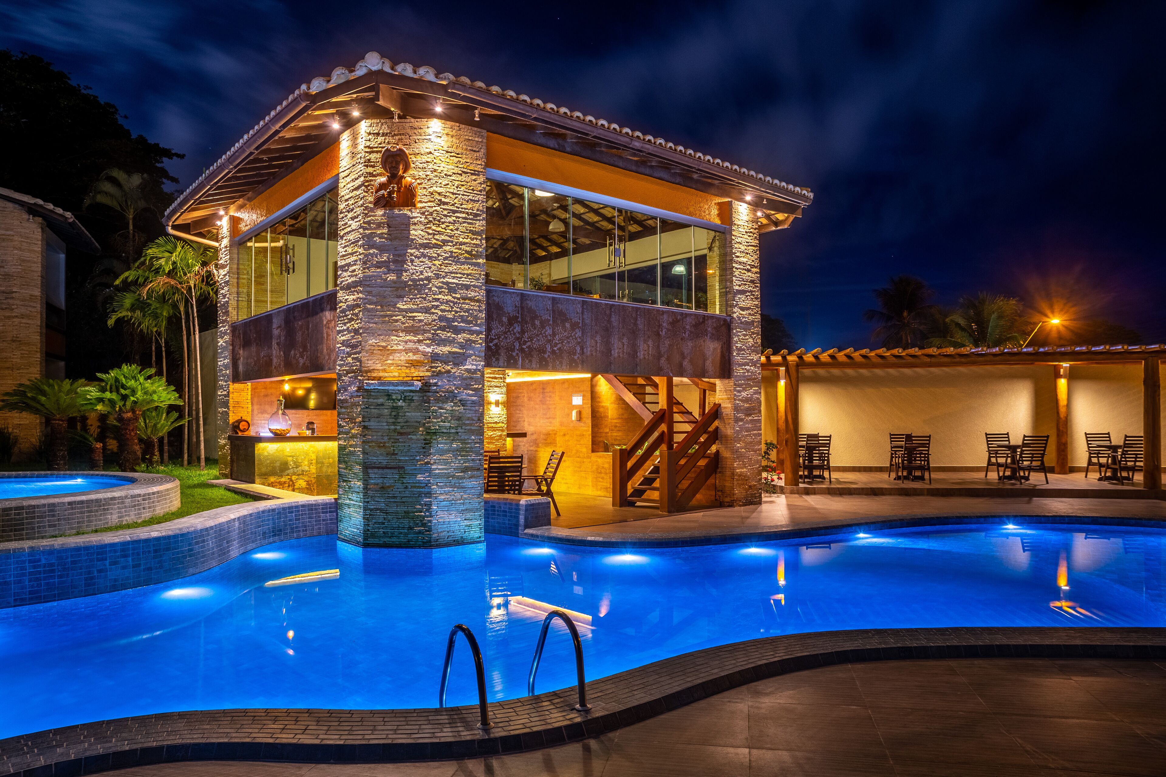 Uma área moderna na piscina, com uma estrutura de pedra, um lounge envidraçado e uma piscina bem iluminada.