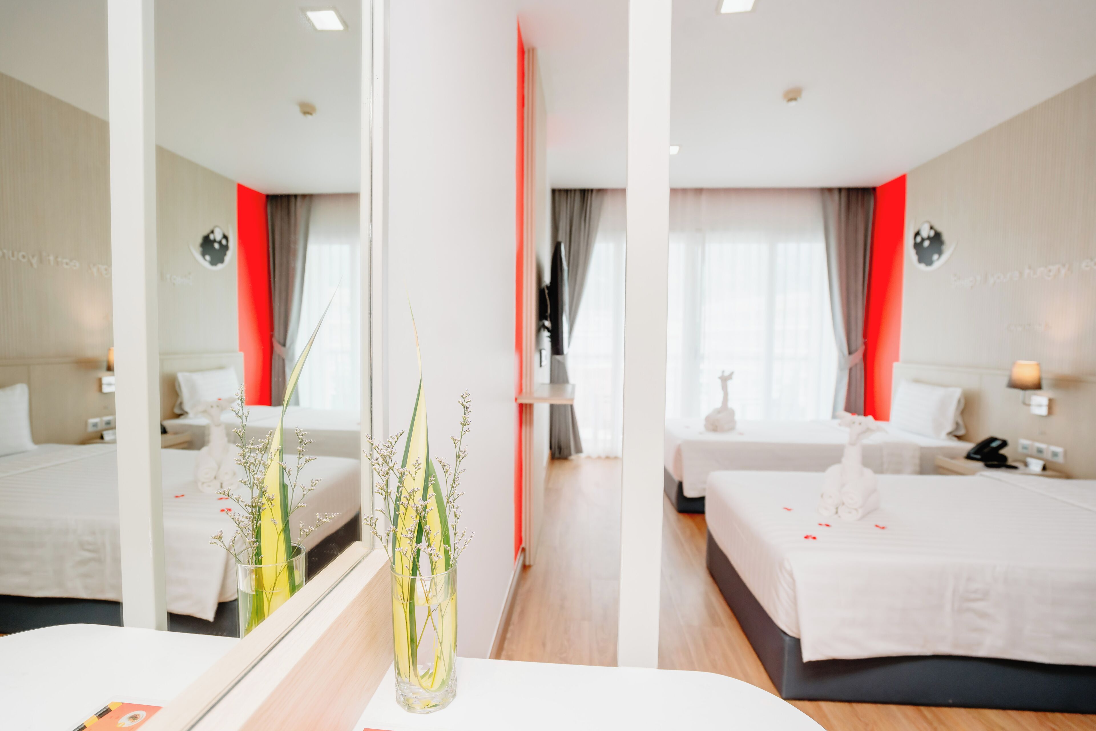 Quarto de hotel com duas camas, um espelho, um vaso com flores e vista para o corredor.