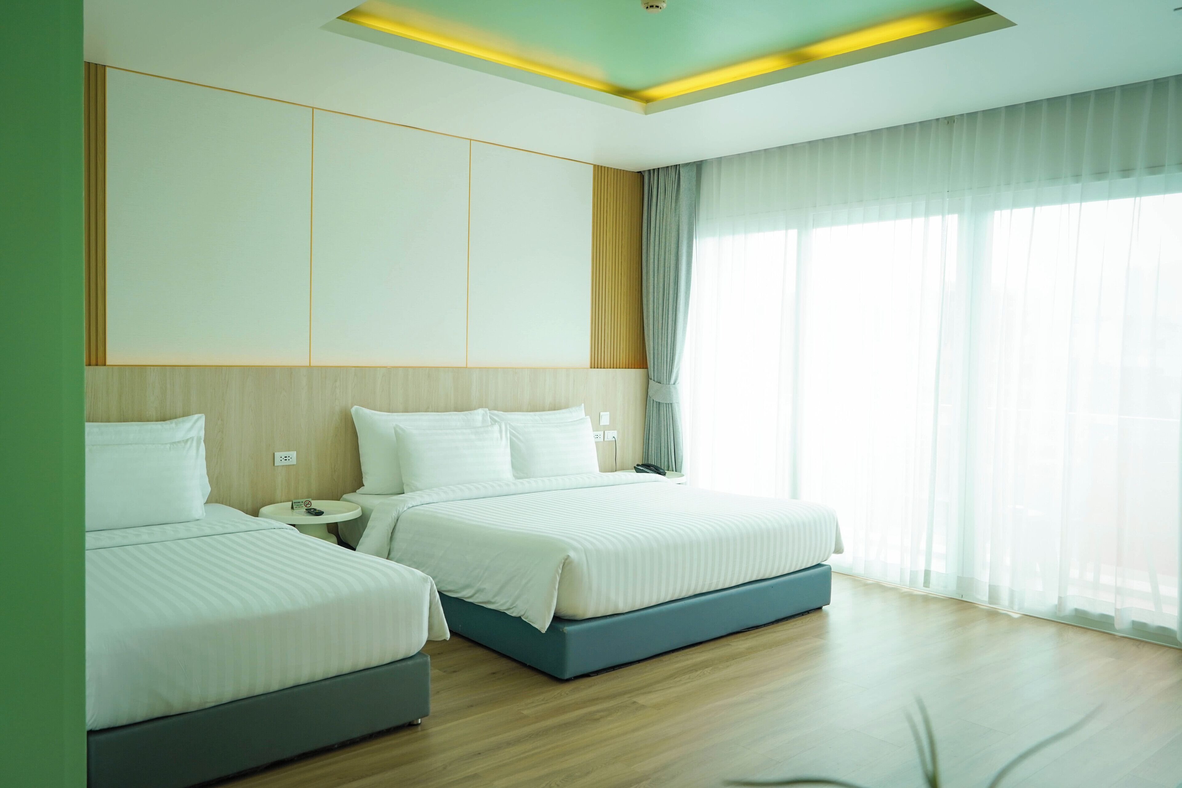 Quarto de hotel com duas camas, mesa de cabeceira, tomada e janela com cortinas.
