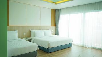 Quarto de hotel com duas camas, mesa de cabeceira, tomada e janela com cortinas.