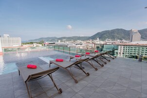 Área de piscina no terraço com espreguiçadeiras e barreira de vidro, com vista para a paisagem urbana e montanhas.