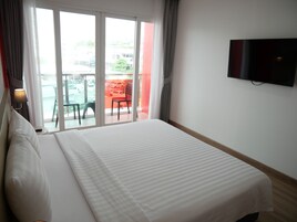 Quarto de hotel com uma cama, televisão fixada na parede e varanda com cadeira e mesa.