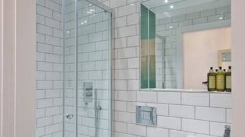 Uma casa de banho moderna com azulejos brancos tipo metrô, cabine de chuveiro em vidro, lavatório branco e espelho sobre o lavatório.
