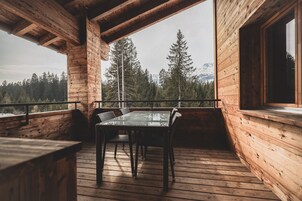 Um deck de madeira com mesa e cadeiras, com vista para uma área montanhosa arborizada.