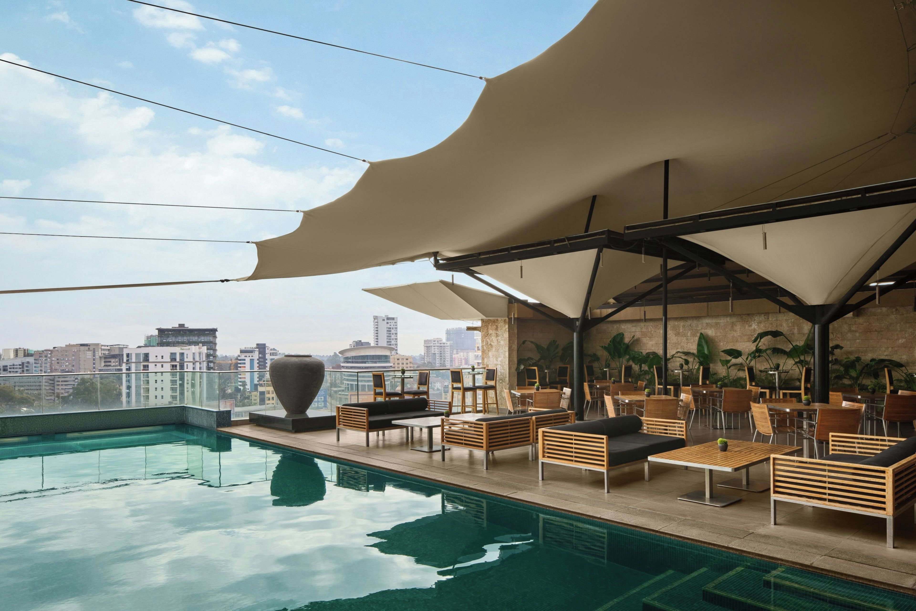 Área de piscina no terraço com vista para o horizonte da cidade, mobiliário de jardim e um vaso decorativo grande.