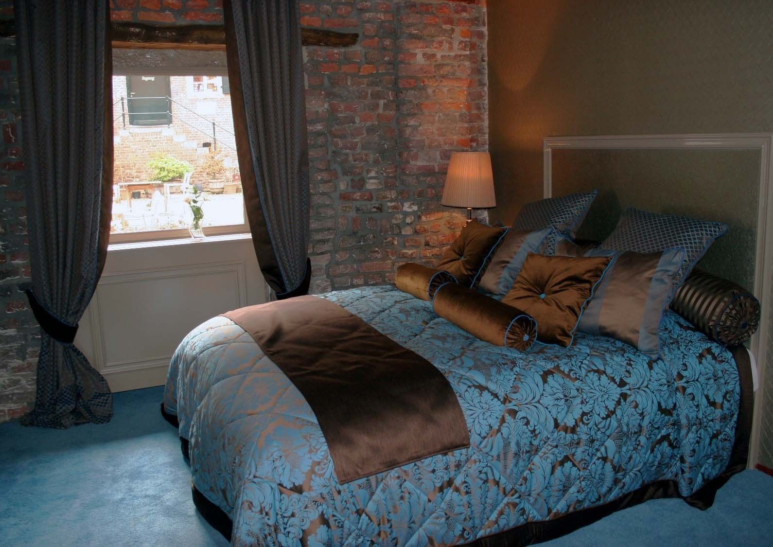 Quarto com parede de tijolos, janela com cortinas, cama com roupa de cama estampada e abajur.
