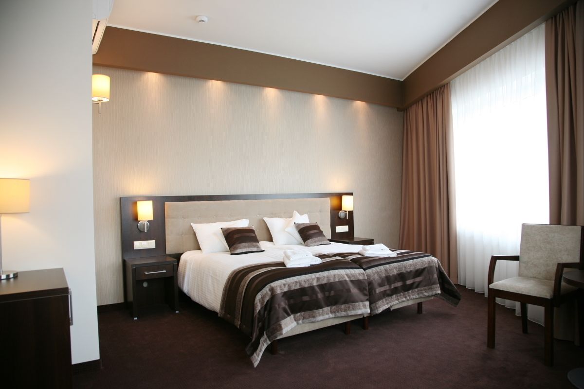 Quarto de hotel com uma cama grande, duas luminárias de cabeceira, uma cadeira e uma mesa de cabeceira.