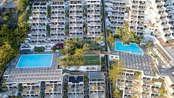 Hotel moderno e alto com várias varandas, piscina central e palmeiras ao redor.