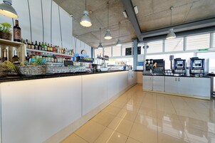 Uma área de bar com um balcão comprido, prateleiras com garrafas e piso revestido de azulejos.