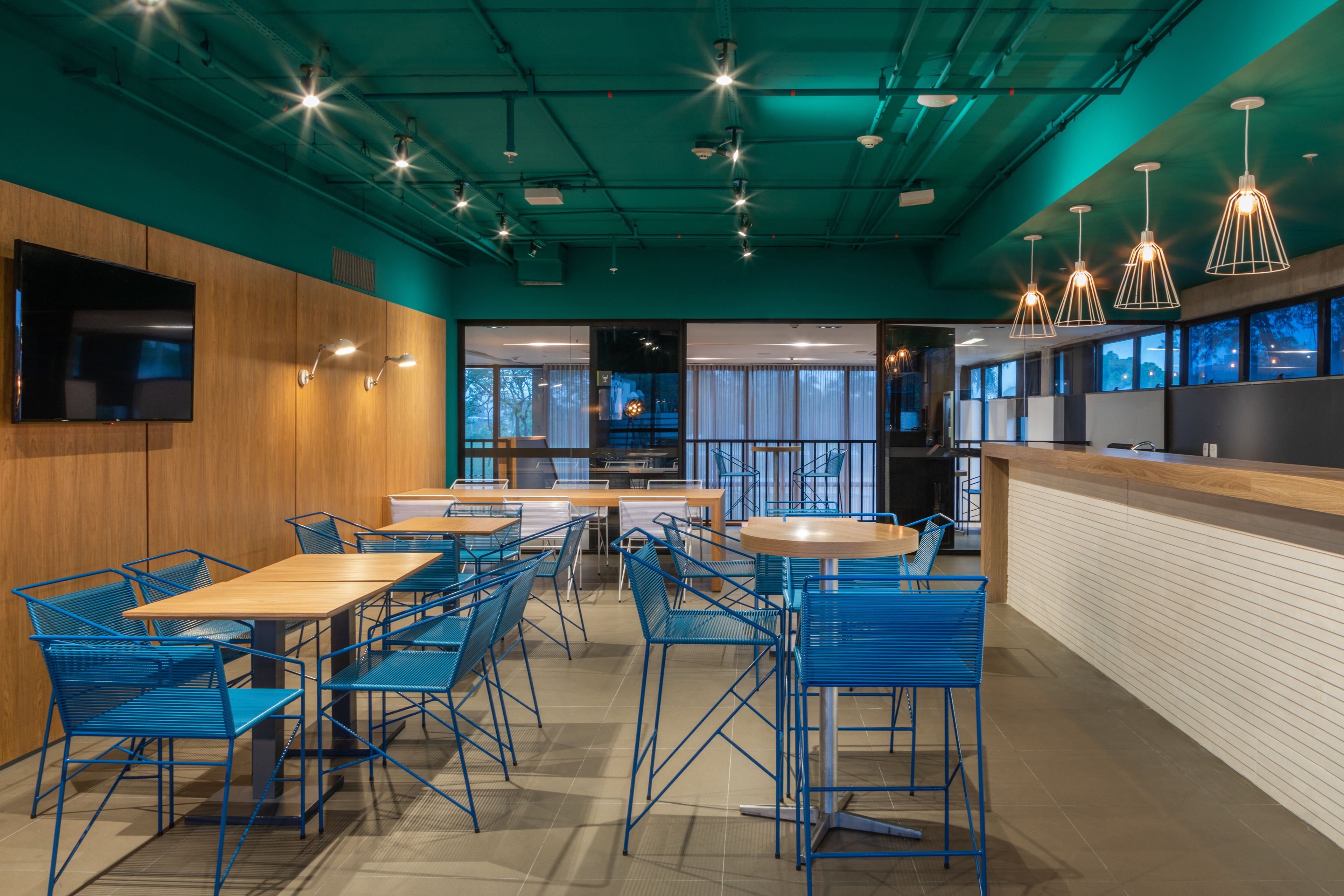 Um restaurante moderno com cadeiras de metal azuis, mesas de madeira e iluminação pendente.