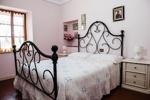 Quarto com cama, mesa de cabeceira, luminária e janela com cortinas.