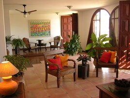 Uma sala de estar ampla, com um banco de madeira, cadeiras e plantas em vasos.