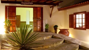Escada que leva a um quarto com porta de madeira identificada com a inscrição “Boqueirão”, cercada por vasos de plantas e uma janela com persianas de madeira.