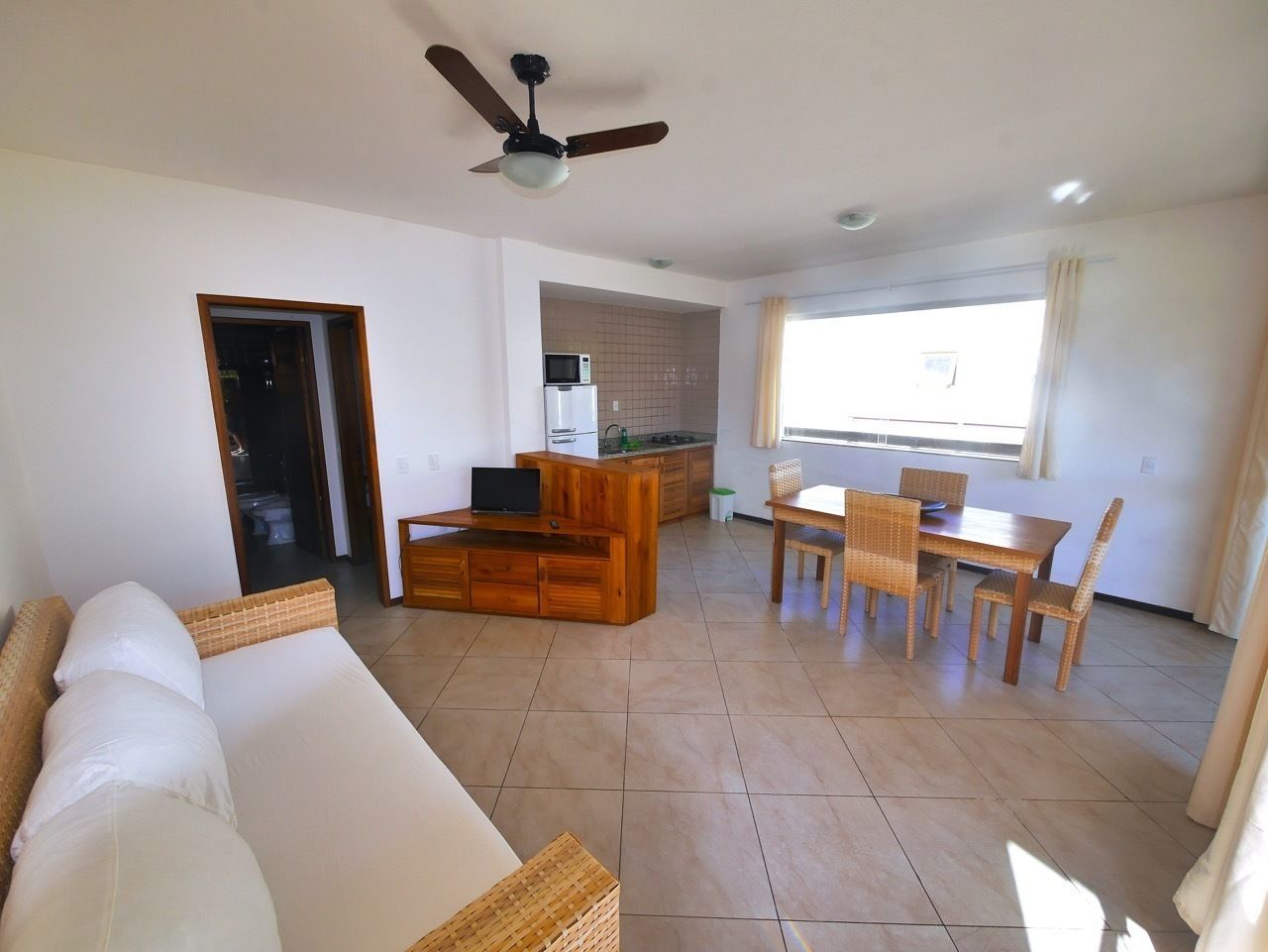 Ampla sala de estar com sofá, mesa de jantar, cadeiras, kitchenette e ventilador de teto.