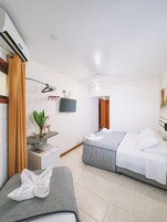 Quarto de hotel com uma cama, um sofá, uma televisão na parede e um ventilador de teto.