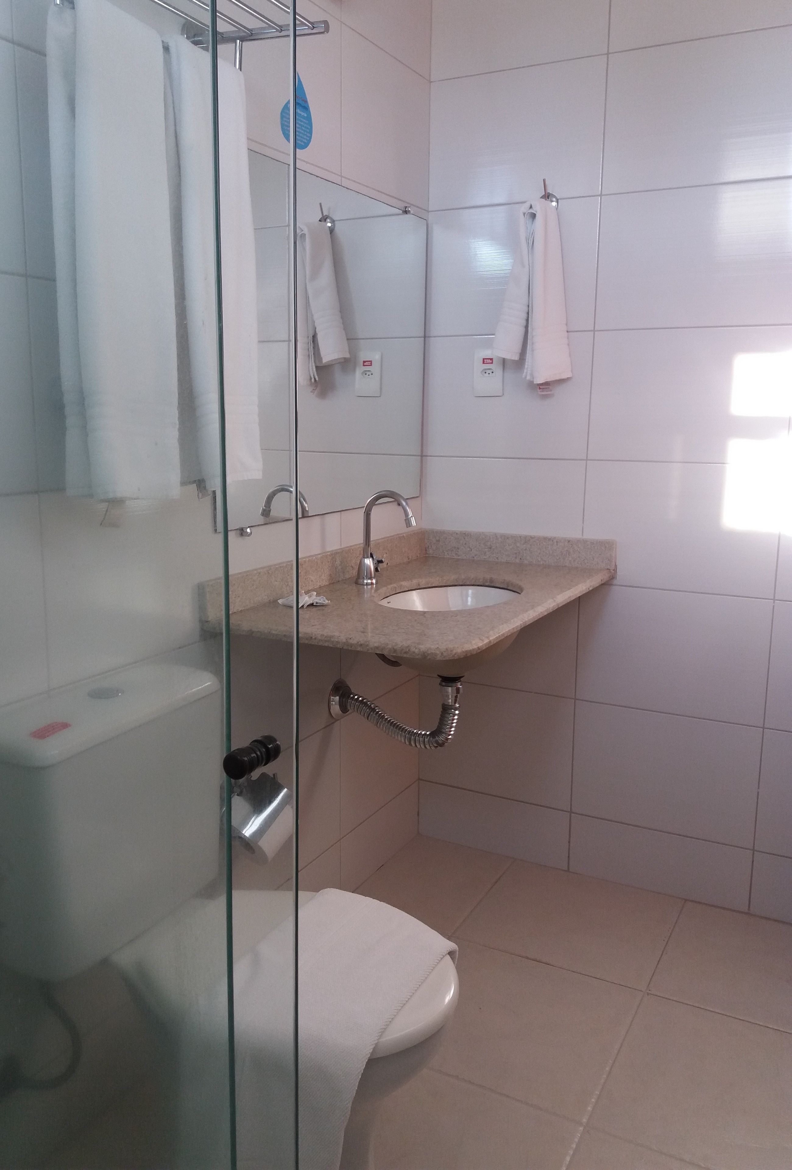 Uma casa de banho com cabine de duche em vidro, lavatório com bancada bege e sanita.