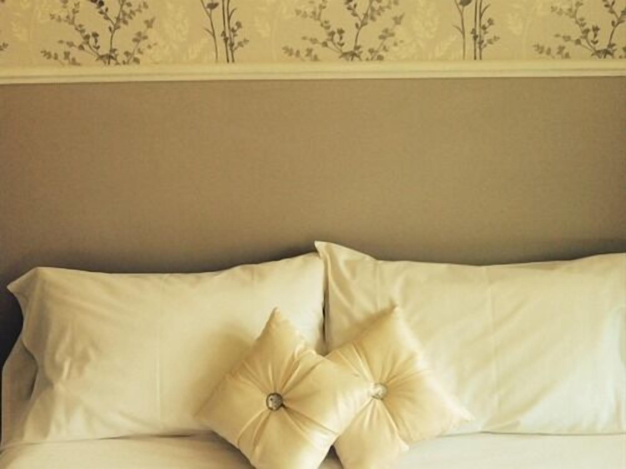 Cama com duas almofadas e papel de parede com padrão floral acima.