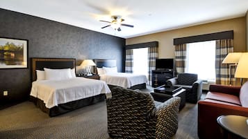 Quarto de hotel com duas camas, ventoinha no teto, televisão e área de estar com sofá e cadeiras.