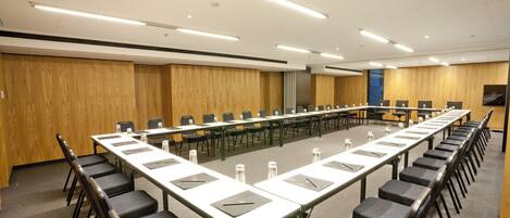 Uma sala de conferências com mesas e cadeiras compridas, painéis de madeira e iluminação embutida.