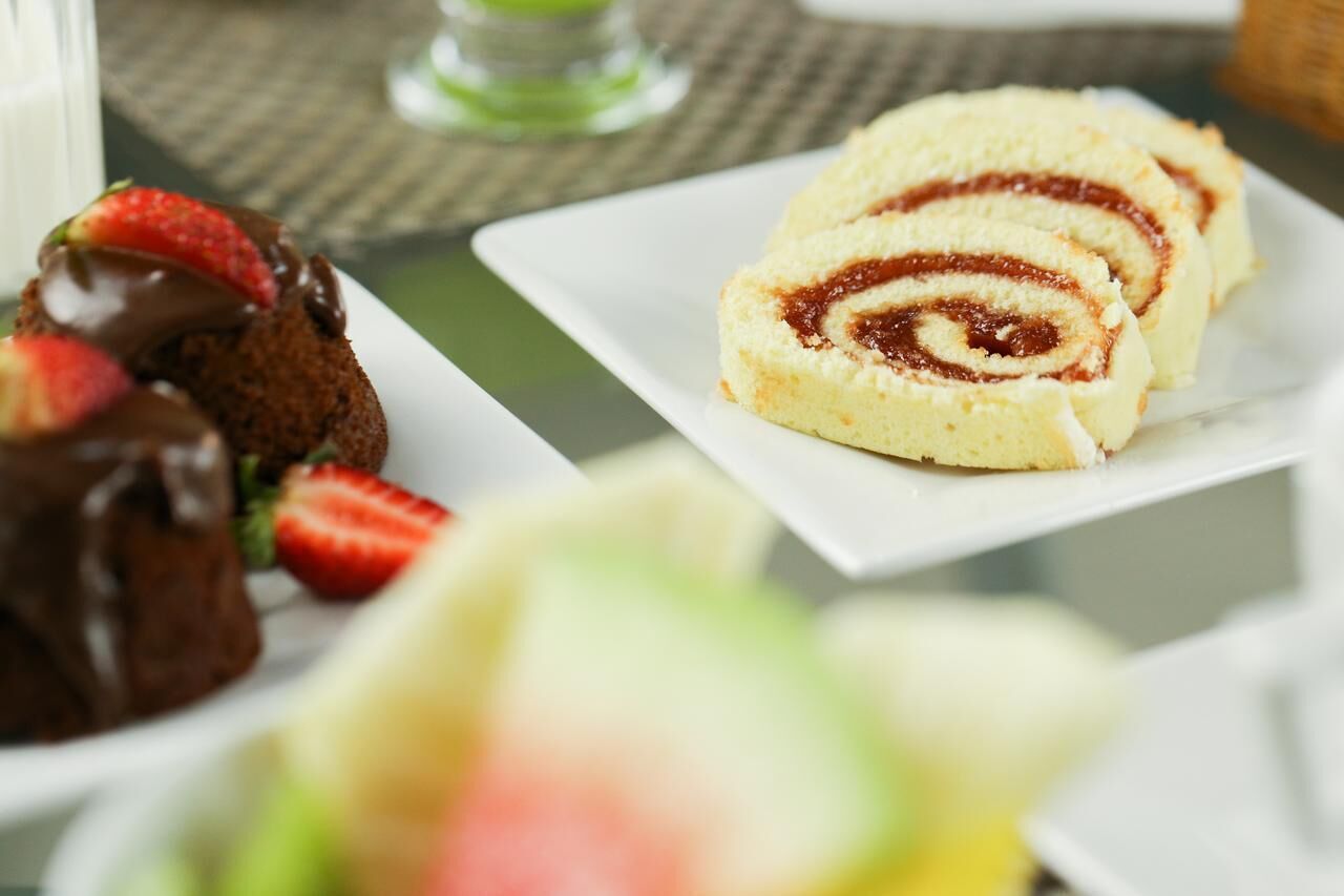 Um prato de sobremesa com um bolo de chocolate e uma morango, e um prato com um doce enrolado.