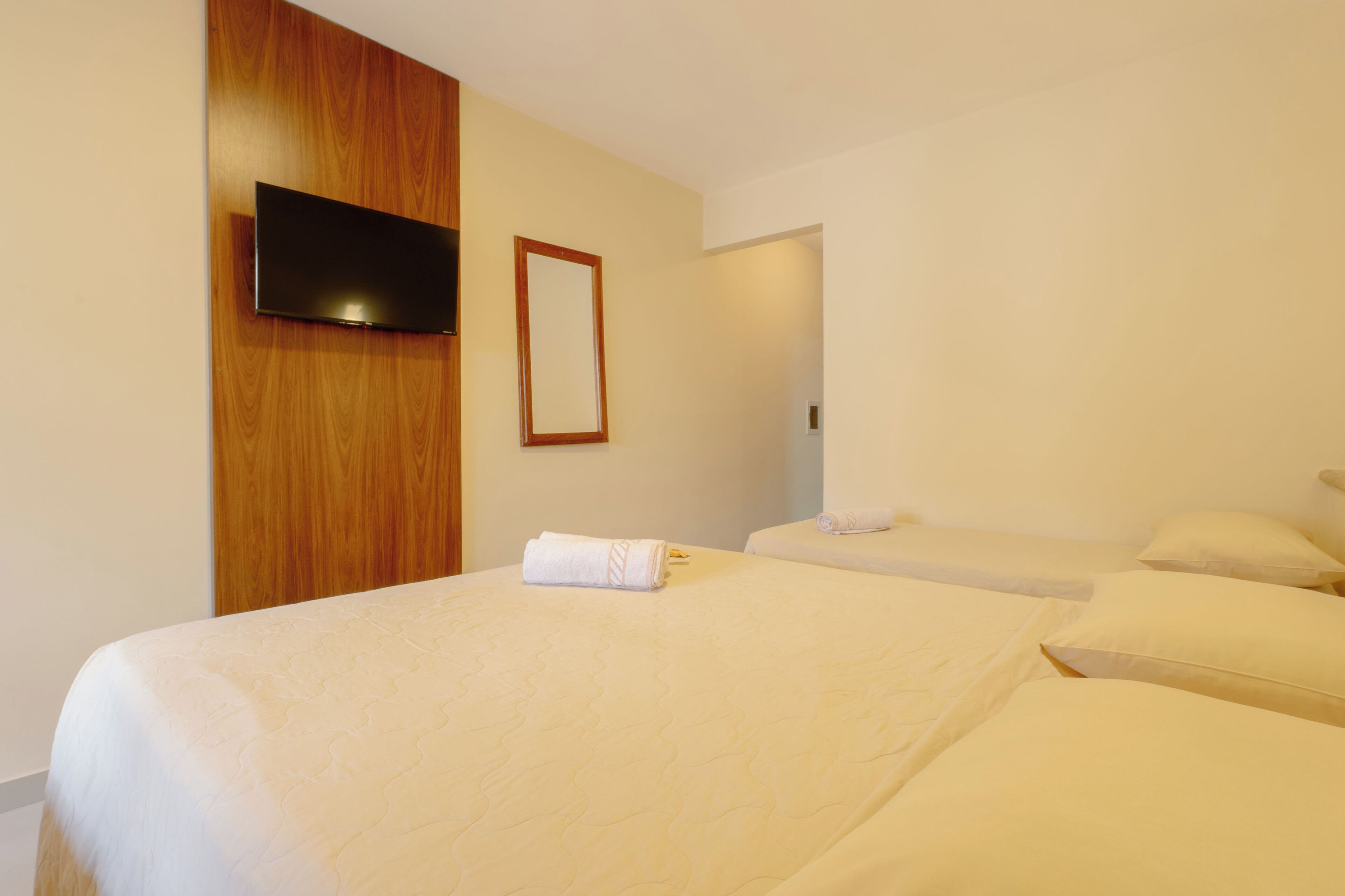 Quarto de hotel com duas camas, televisão de tela plana presa na parede e painel de madeira.