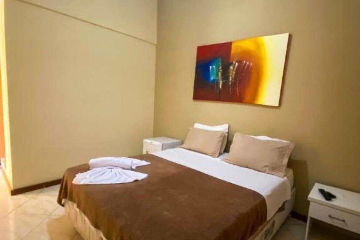 Quarto de hotel com cama, mesa de cabeceira, ventoinha no teto e um quadro na parede.