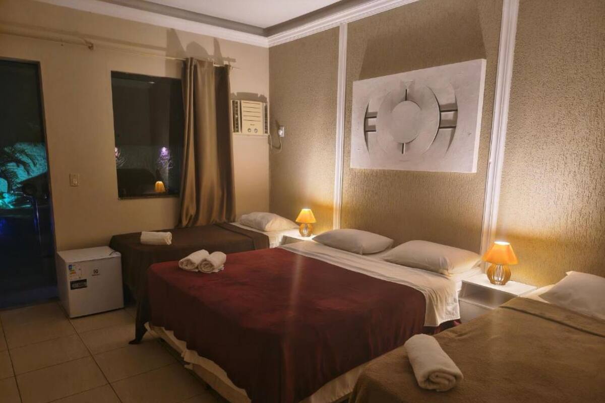 Quarto de hotel com duas camas, ar condicionado na parede, televisão e um pequeno aquecedor.