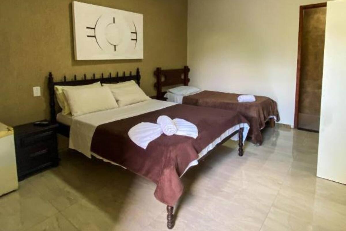 Quarto de hotel com duas camas, um relógio na parede e uma porta à direita.