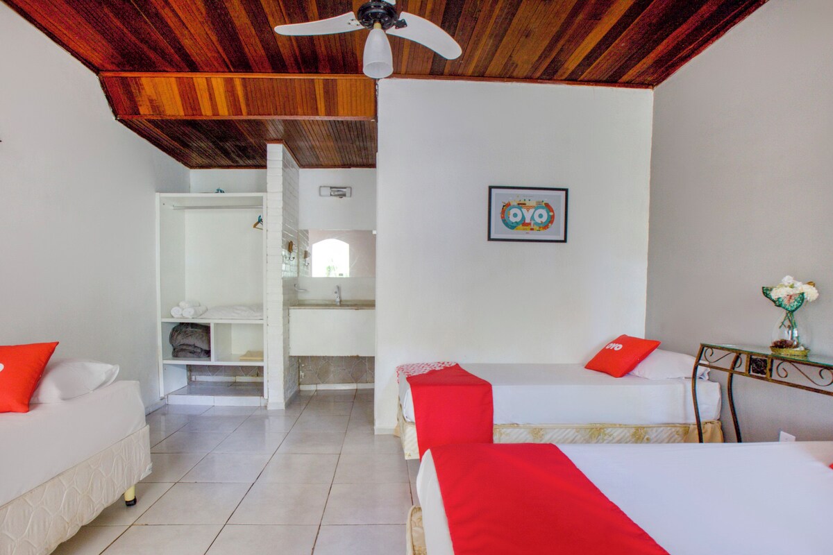 Quarto de hotel com duas camas, um ventilador de teto, banheiro com espelho e um quadro na parede.