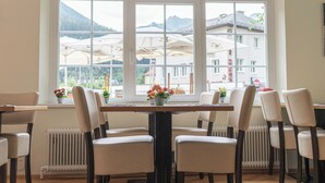Uma área de jantar com uma grande janela em arco, cadeiras brancas, uma mesa de madeira e um vaso de flores.