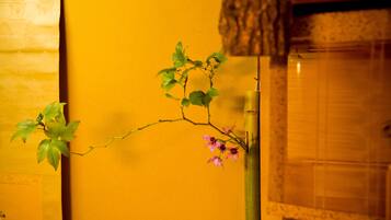 Uma planta com folhas verdes e flores cor-de-rosa em frente a uma parede amarela.