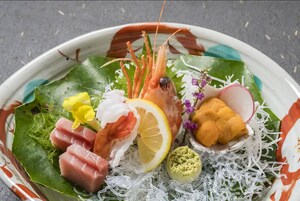 Uma tigela de sashimi com diversos acompanhamentos, incluindo uma cauda de lagosta, limão e rabanete.