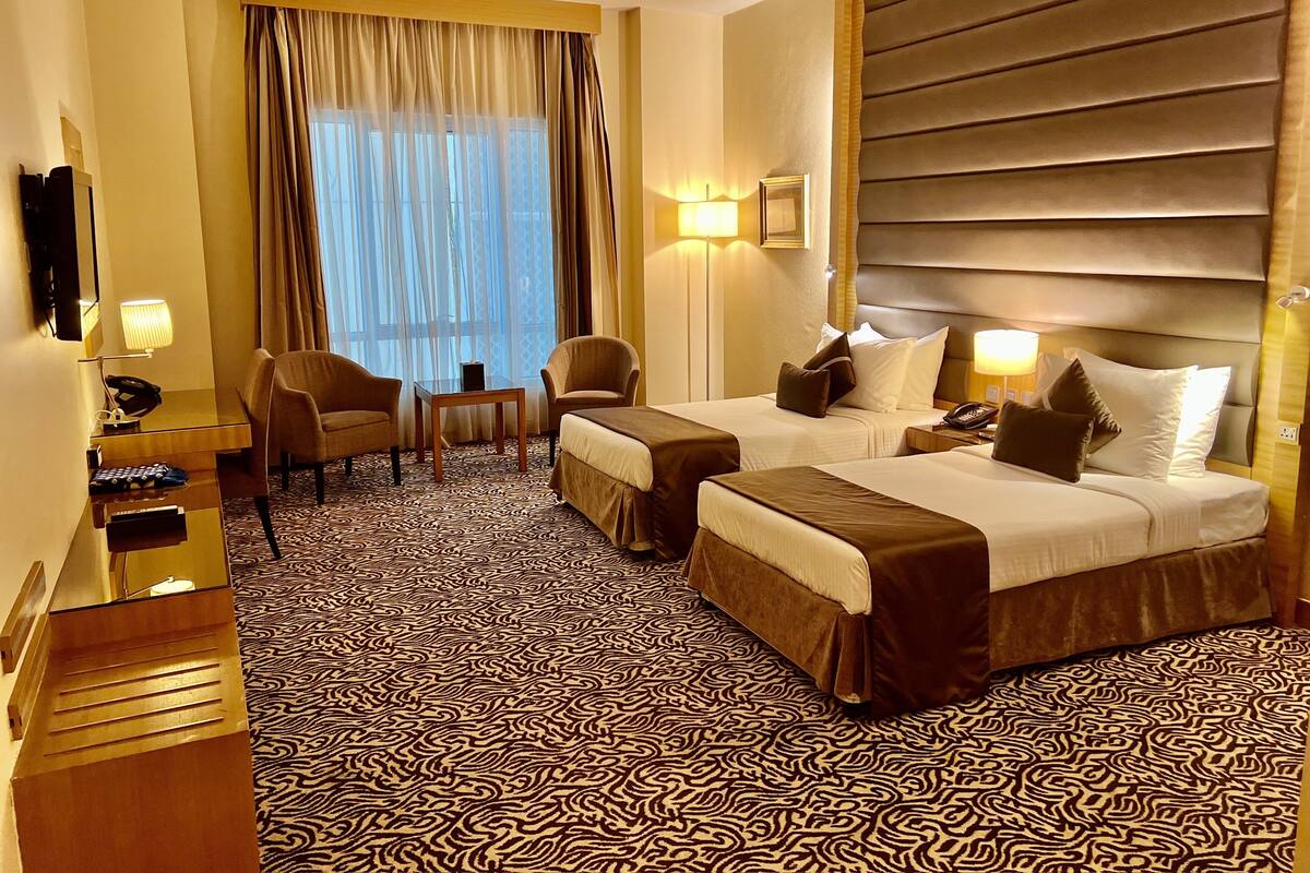Quarto de hotel com duas camas, uma escrivaninha, uma cadeira e uma televisão.