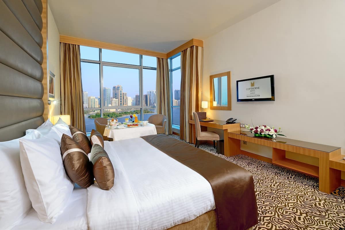 Quarto de hotel com uma cama grande, uma escrivaninha, uma cadeira e vista para a paisagem urbana.