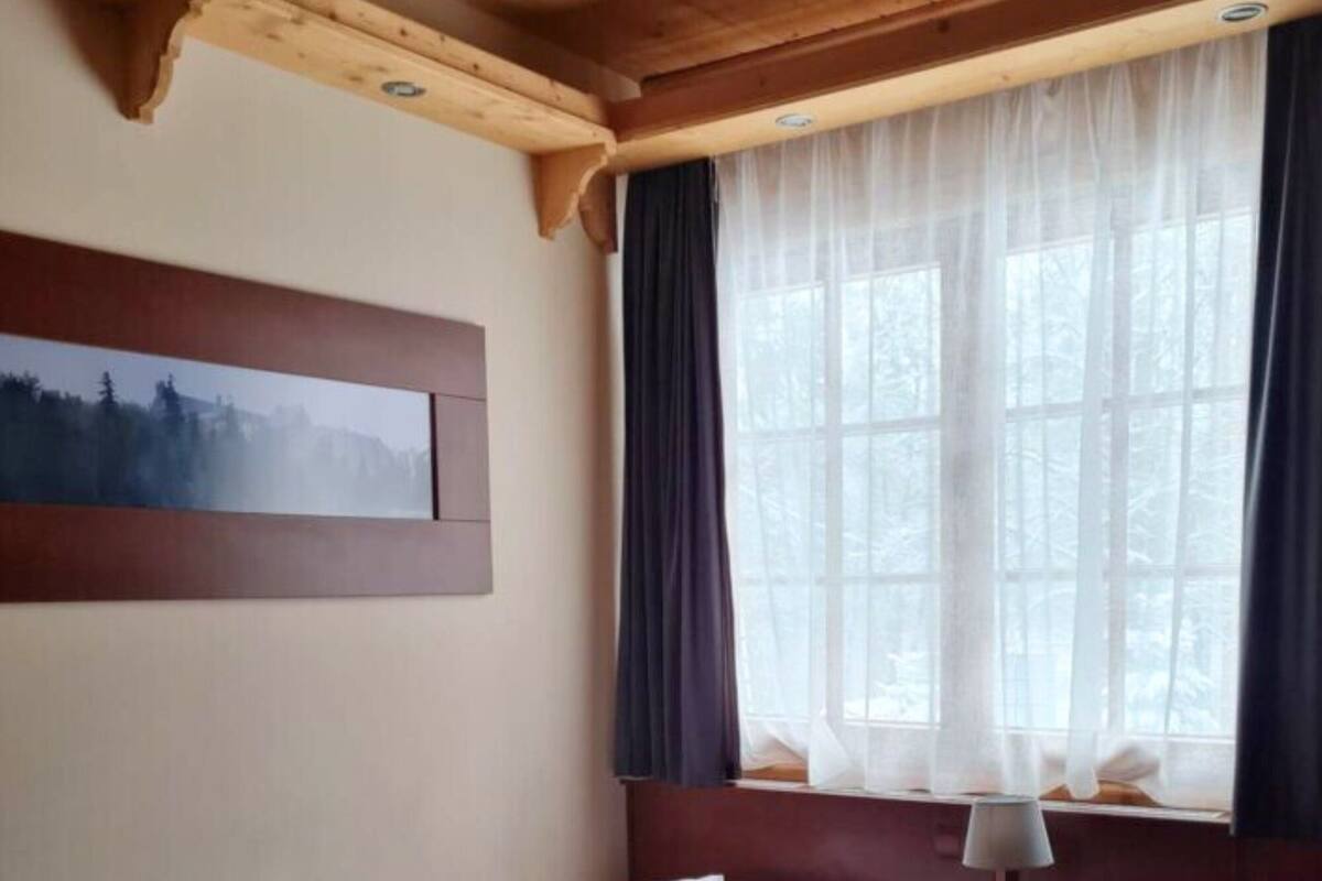 Quarto pequeno e acolhedor com uma cama de solteiro, mesa de cabeceira, abajur e janela com cortinas.