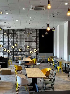 Uma área de jantar moderna com várias mesas e cadeiras, parede com padrão e iluminação pendente.