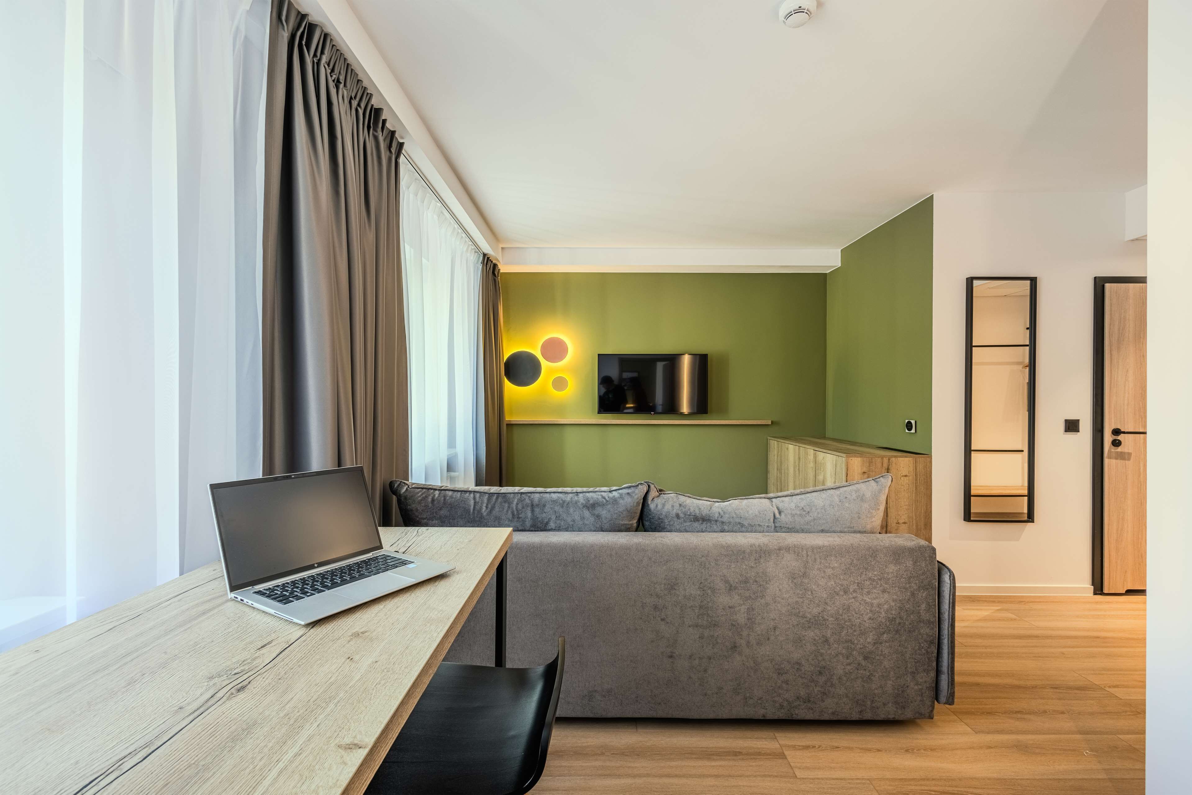 Uma sala de estar moderna com um sofá, uma mesa de madeira com um laptop e uma televisão fixada na parede.