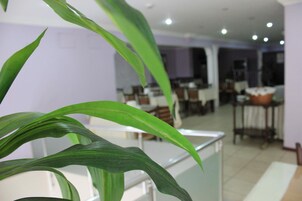 Interior moderno com área de refeições, cozinha e uma planta em vaso no primeiro plano.
