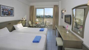 Quarto de hotel com duas camas, uma escrivaninha, uma cadeira, uma mesinha, um espelho e vista para o exterior.