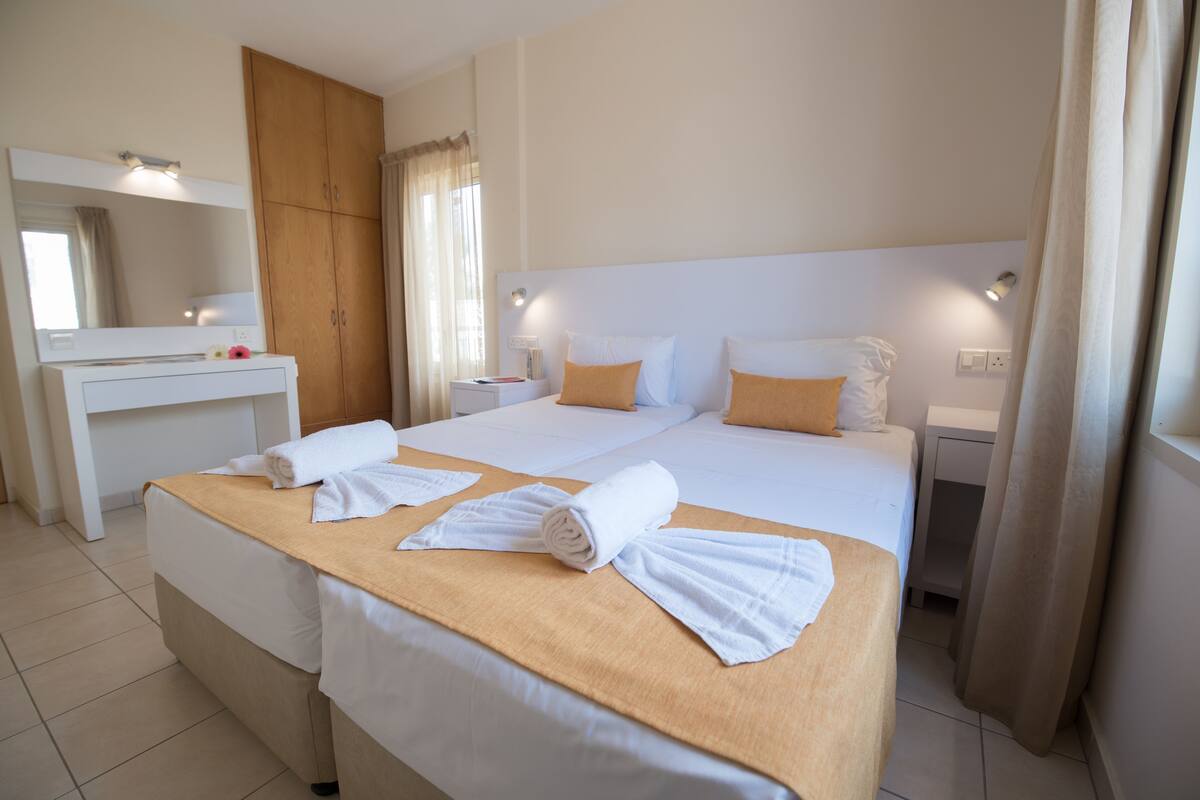 Quarto de hotel com uma cama grande, uma mesinha de cabeceira, um espelho e um guarda-roupa.