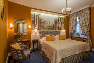 Quarto de hotel com cama grande, uma cadeira, um espelho e um mural na parede.