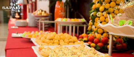 Uma mesa de buffet com diversos alimentos, incluindo cupcakes, donuts e frutas.
