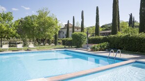 Uma piscina com água azul cristalina, rodeada por vegetação e um edifício ao fundo.