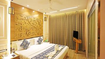Quarto de hotel com uma cama grande, televisão de tela plana, ventilador de teto e painel decorativo na parede.