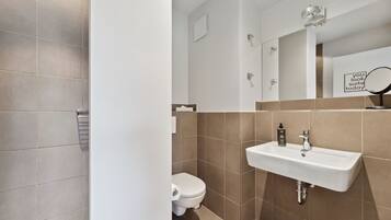 Uma casa de banho moderna com sanita branca, lavatório com espelho em cima e zona de duche.