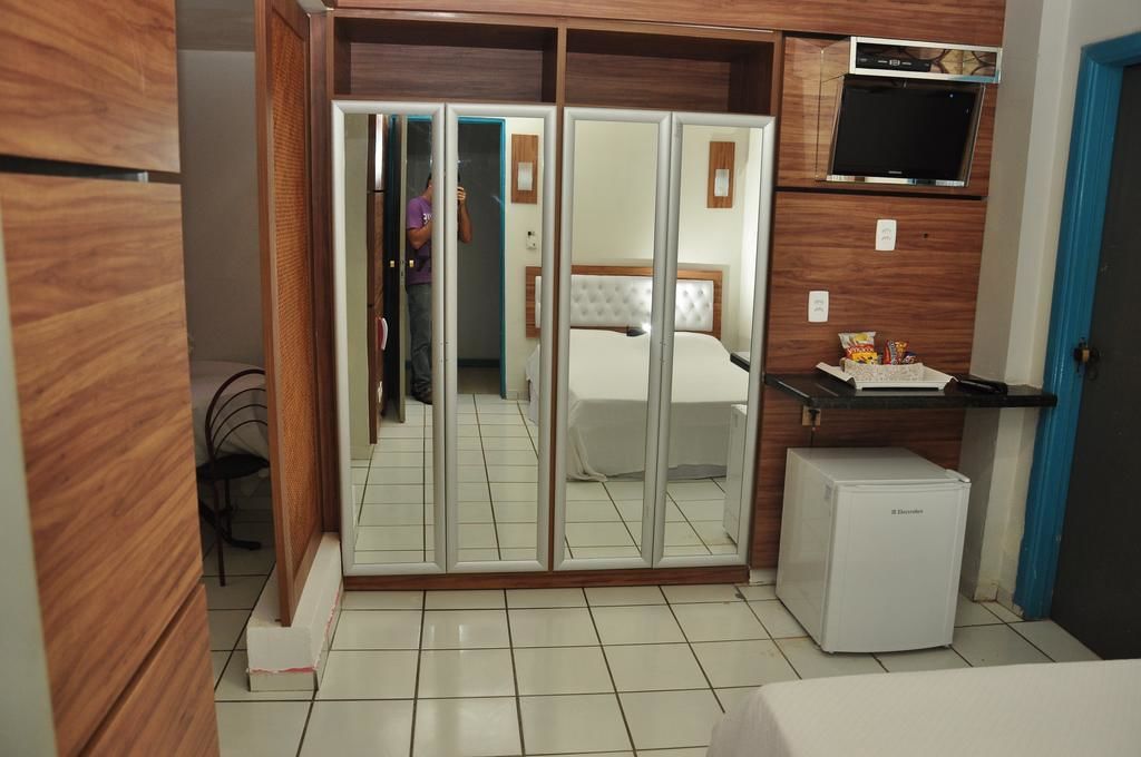 Quarto de hotel com guarda-roupa, cama, televisão e pequeno frigorífico.
