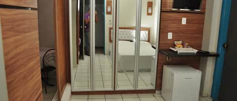 Quarto de hotel com guarda-roupa, cama, televisão e pequeno frigorífico.