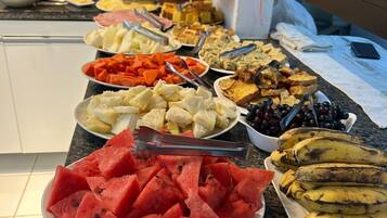 Uma mesa de buffet com diversos alimentos, incluindo frutas, queijos e pão.