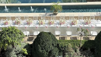 Uma área externa de refeições com mesas preparadas para um evento formal, rodeada por vegetação e uma piscina.