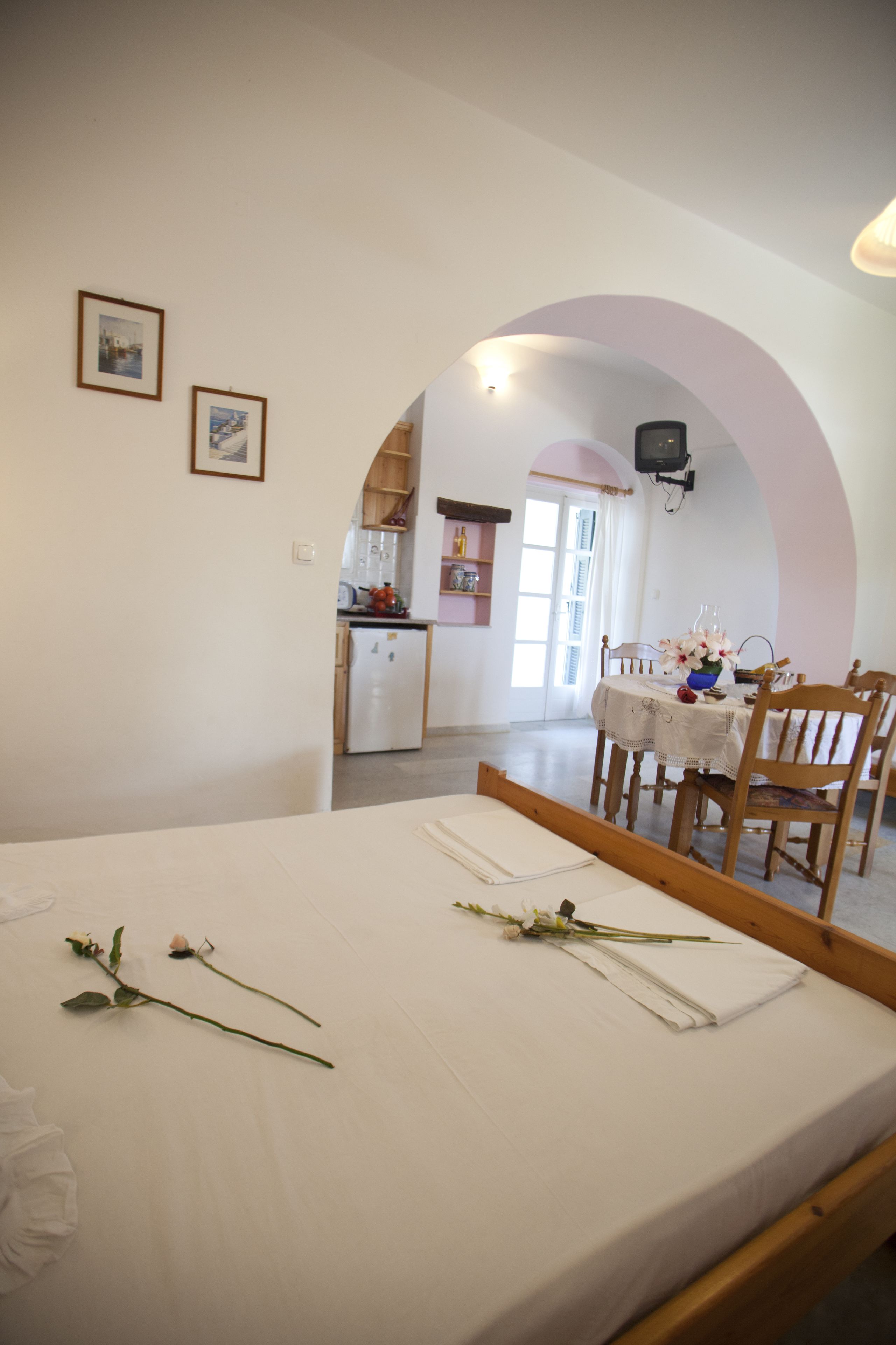 Quarto com cama, uma cadeira de madeira, mesa de jantar com cadeiras, cozinha ao fundo e um corredor.